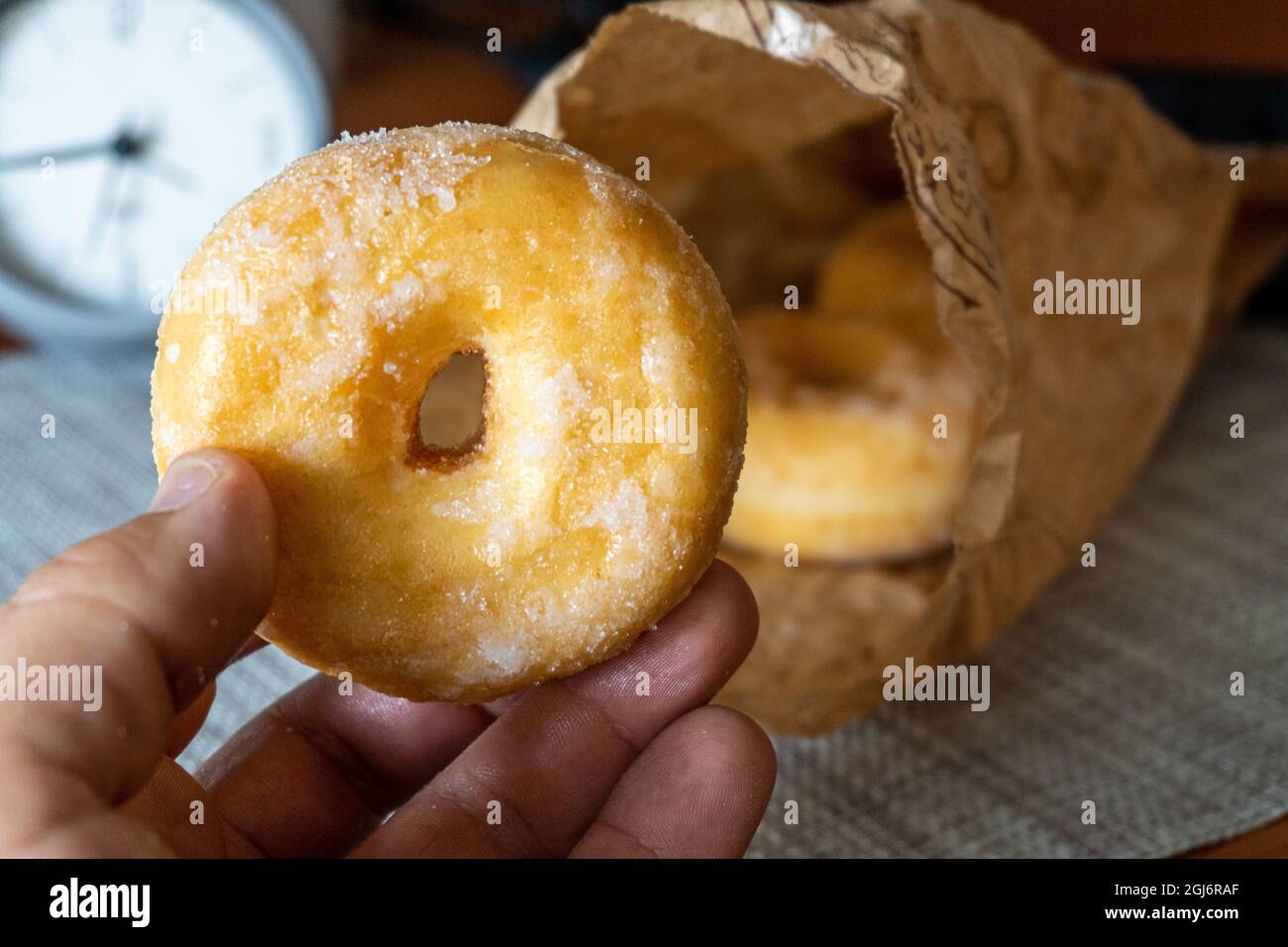 Man's hand holding a glazed donut with a clock and an office background ...
