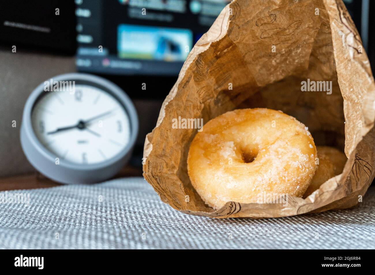 Man's hand holding a glazed donut with a clock and an office background ...
