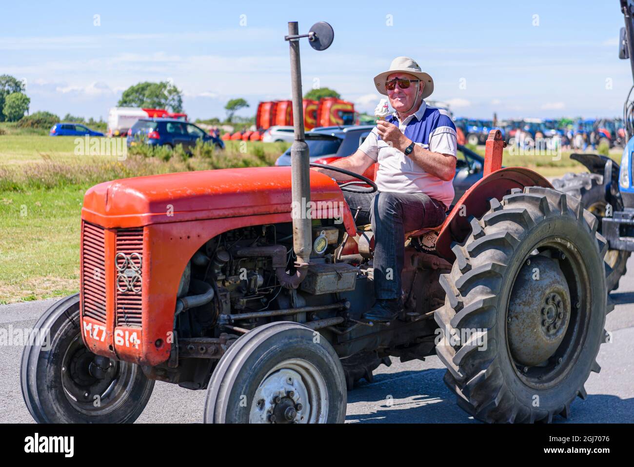 A farmer eats an ice-cream cone while triving a very old red tractor ...