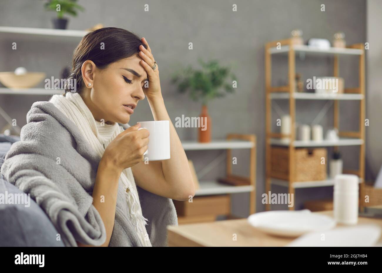 Sick woman who has bad cold or flu fever is sitting on sofa and ...