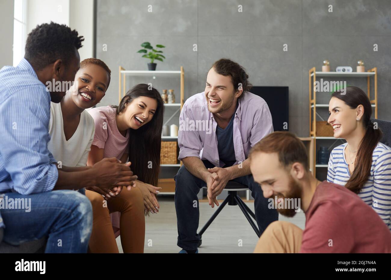 Group of happy young friends sitting in the living-room and laughing at ...
