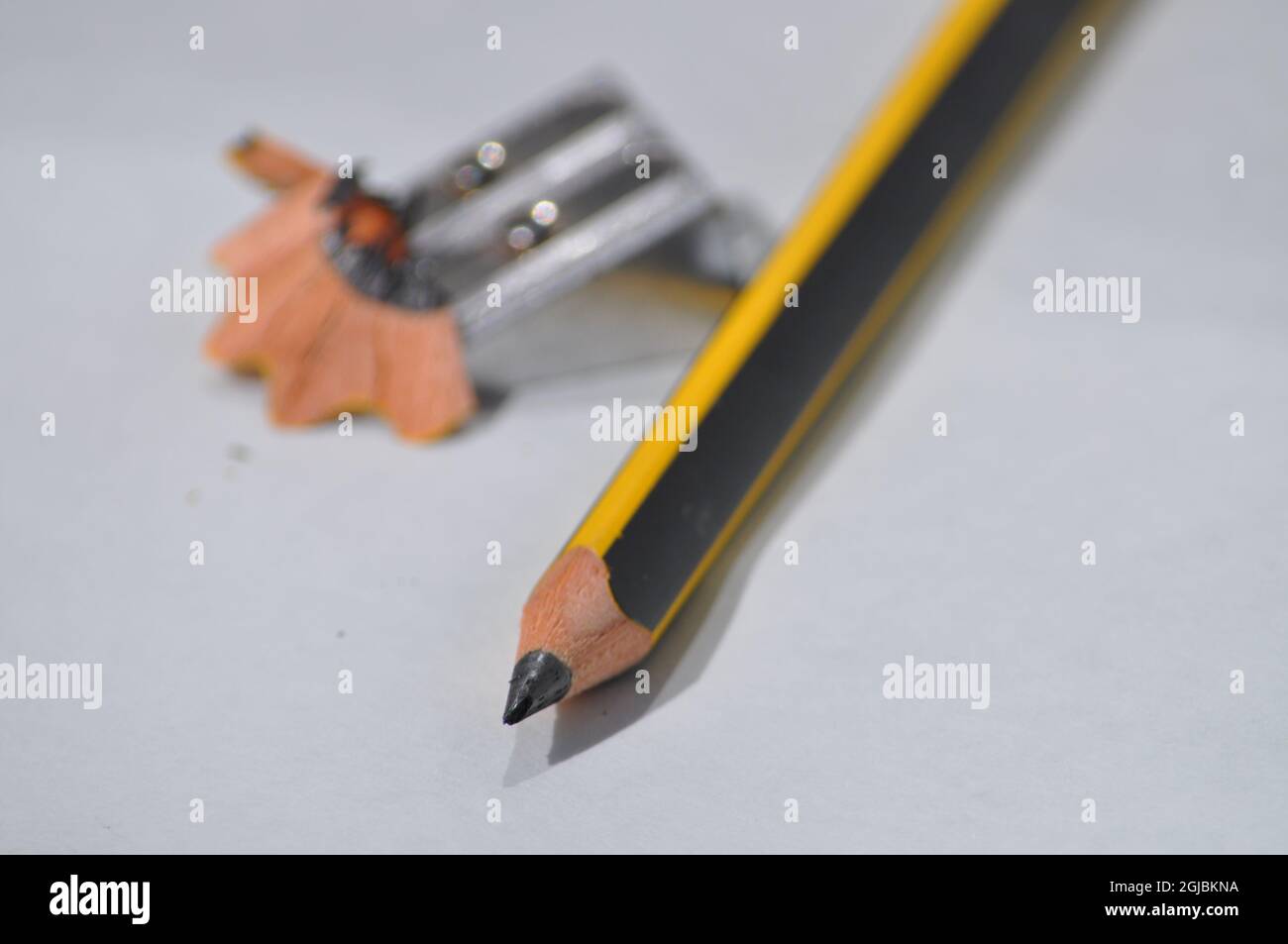 A jumbo HB triangular pencil in focus with a pencil sharpener and ...