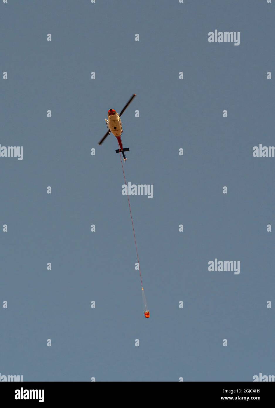 Firefighting helicopter with water bucket on way to drop water onto ...