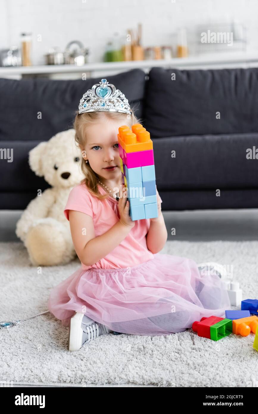 girl in toy crown showing tower of multicolored building blocks while ...
