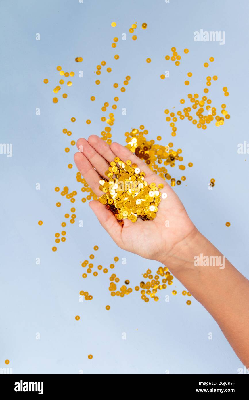 Hands holding golden confetti against blue background, selective focus ...
