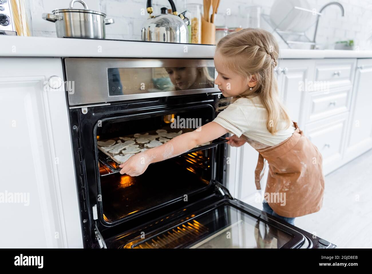 girl in apron placing baking sheet with cookies in oven Stock Photo - Alamy