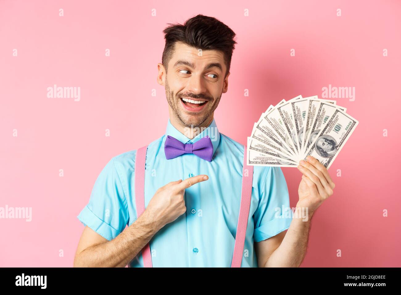 Rich handsome man in festive outfit pointing at money, holding dollars ...