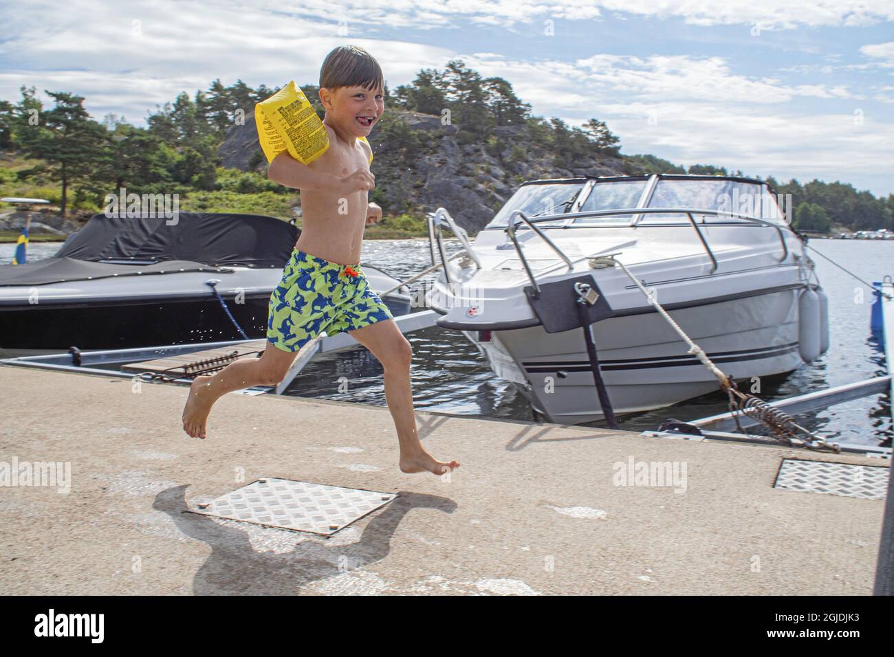 Boy with arm puffs, arm bands, floating devices running on a jetty in ...
