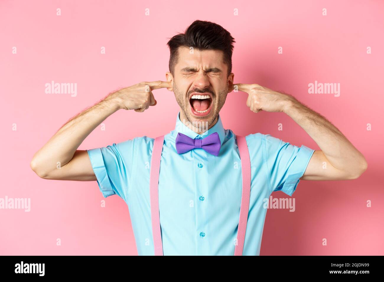 Irritated young man block noise, shut ears with hands and screaming ...