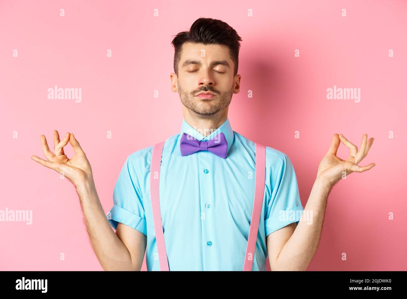 Young guy in bow-tie standing calm and peaceful, meditating with hands ...
