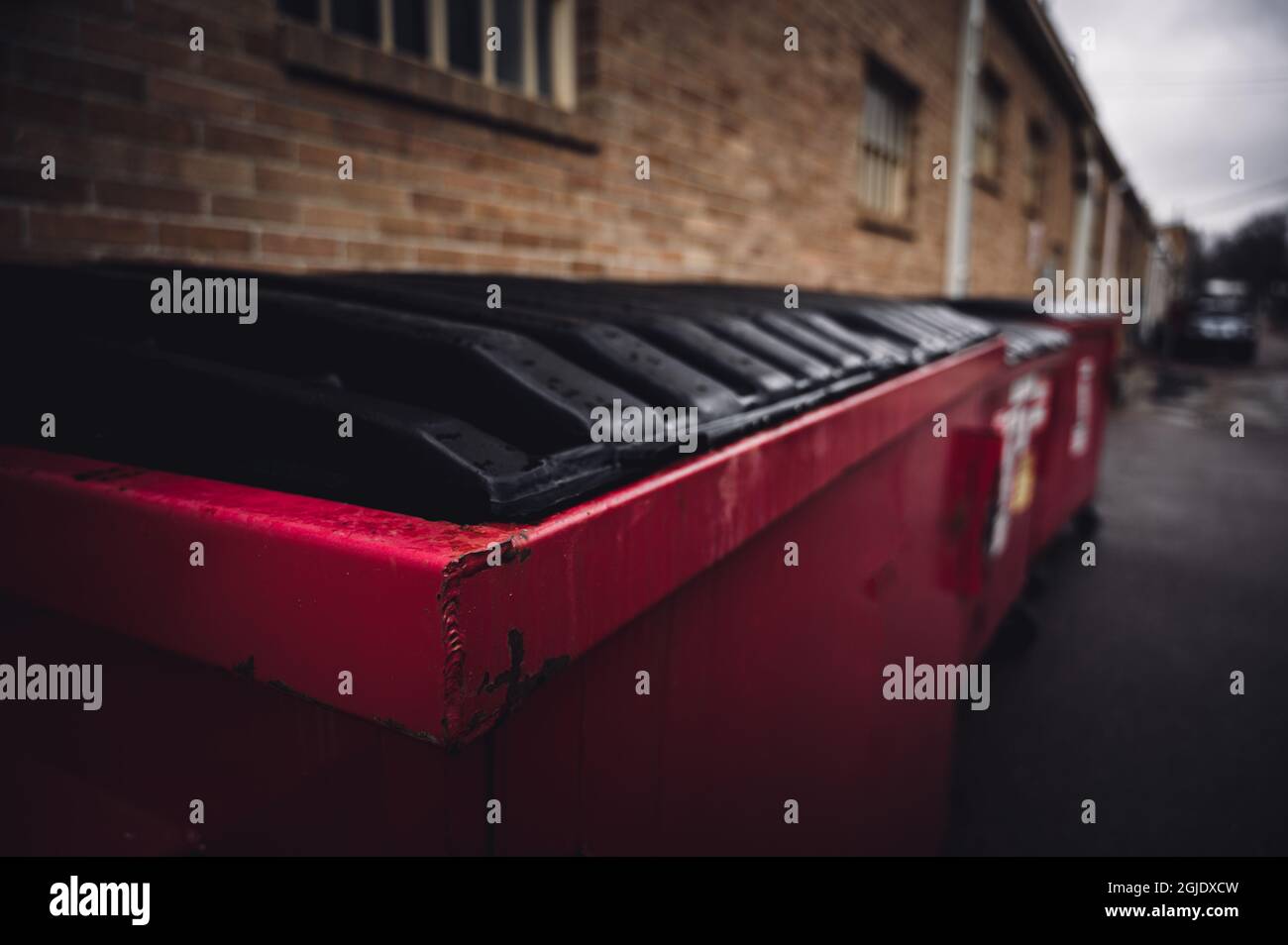 row of covered garbage bins along a brick wall in a back alley Stock ...