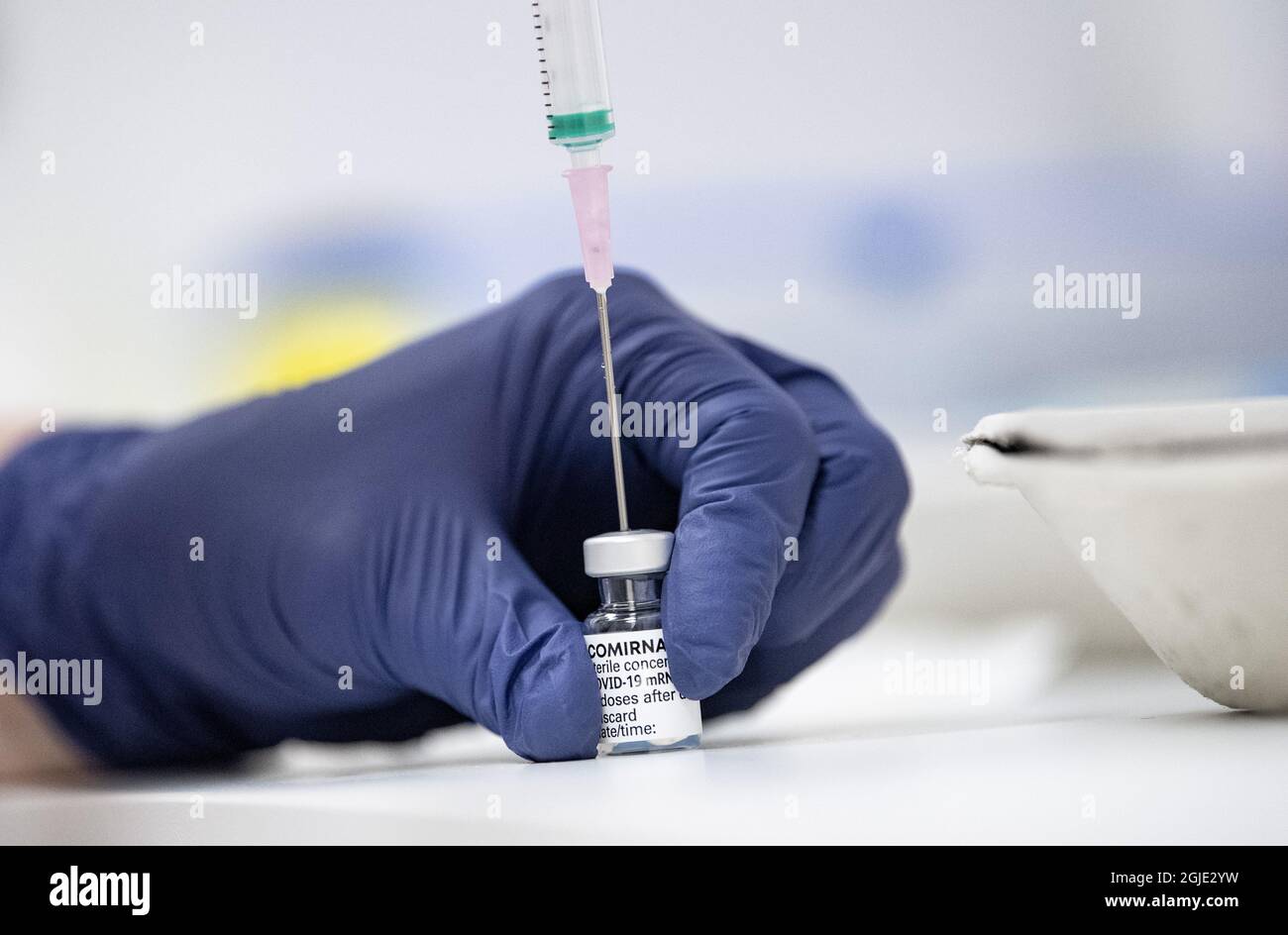 Gloved hands preparing a syringe with Comirnaty Covid-19 vaccine made ...