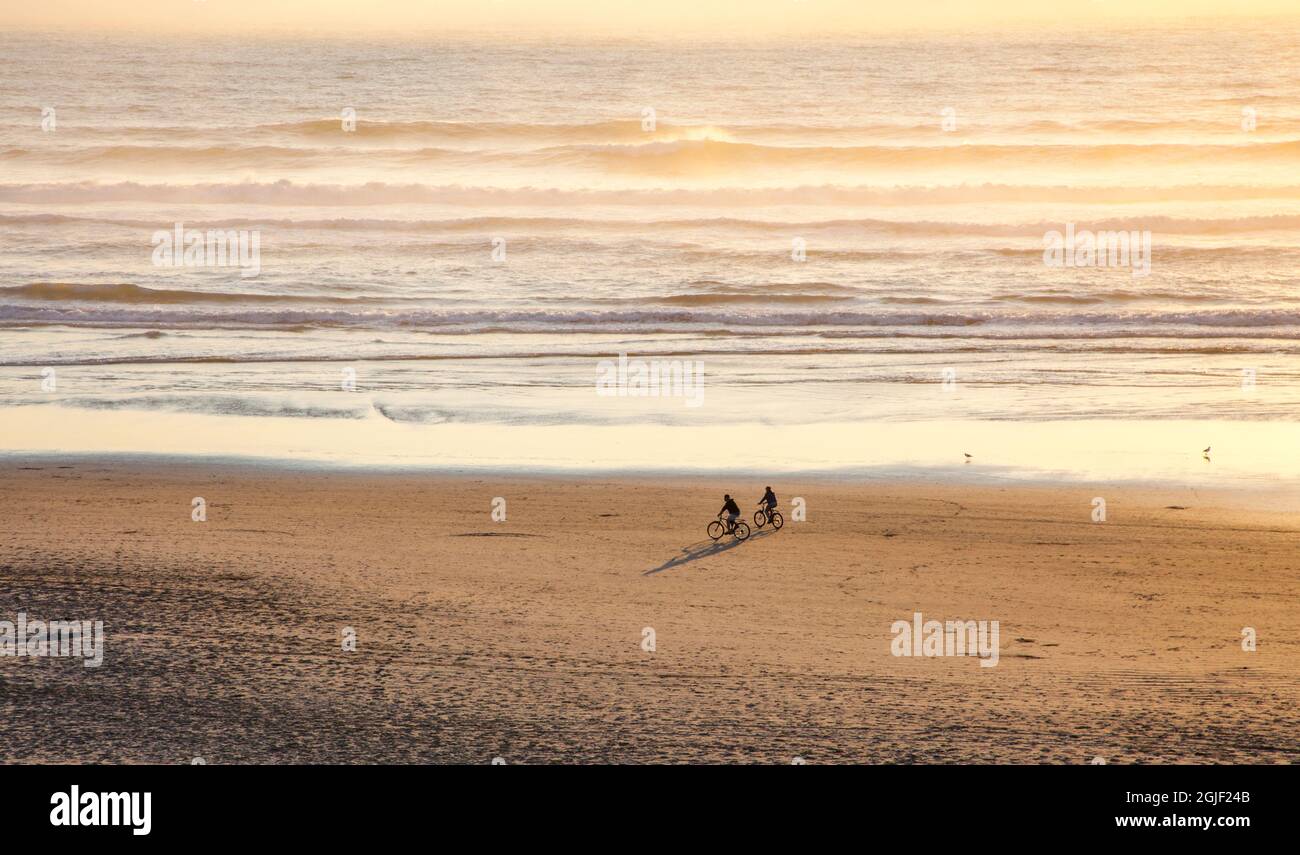 USA, Oregon, Cape Arch with two riding bikes on the beach in the ...