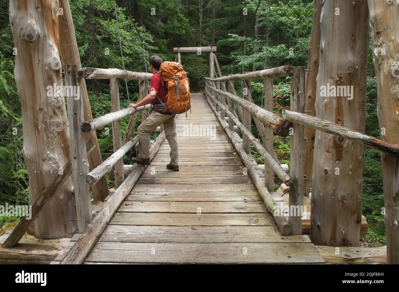 USA, Washington State. Backpacker on suspension bridge over Canyon ...