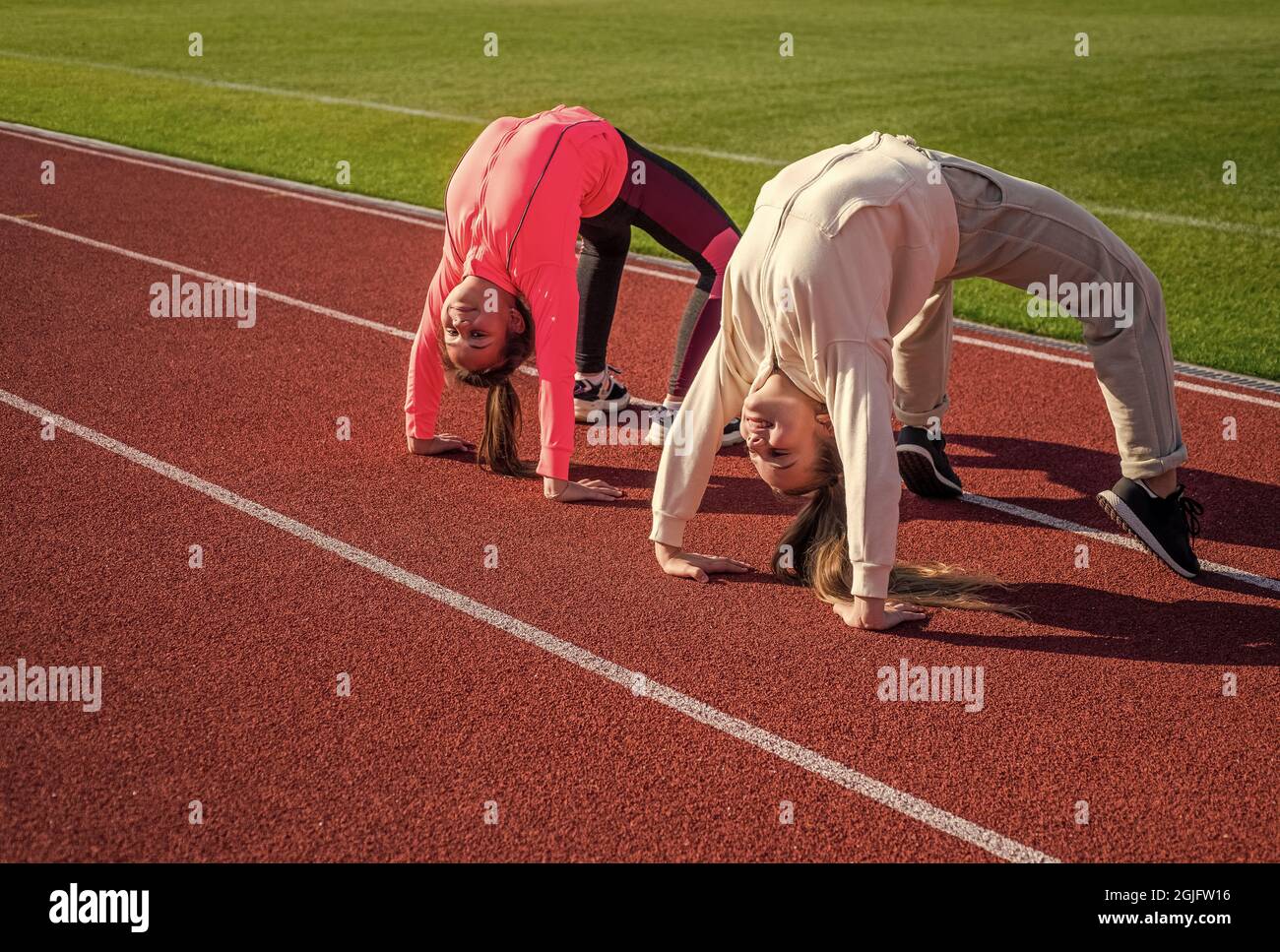 Flexible girls gymnasts stand in crab position on athletics track ...