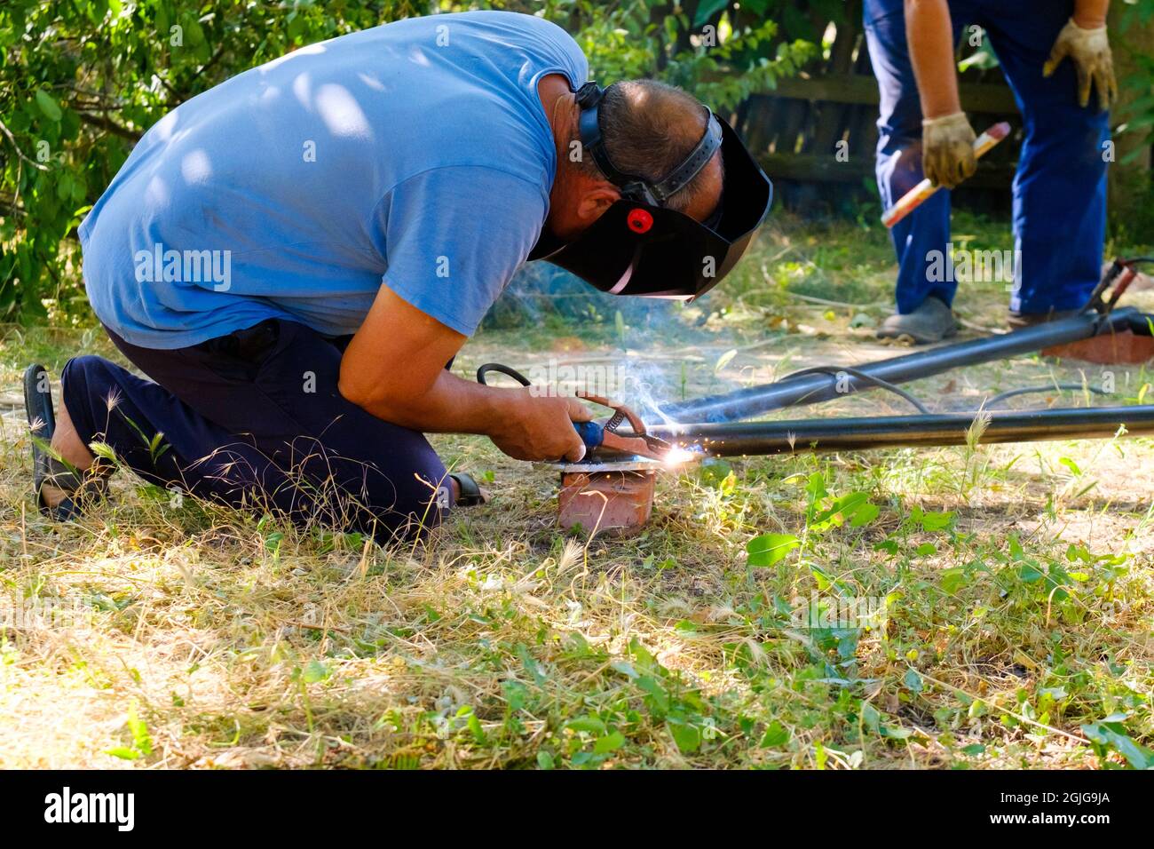 A worker wearing a protective mask welds metal pipes with electric arc ...