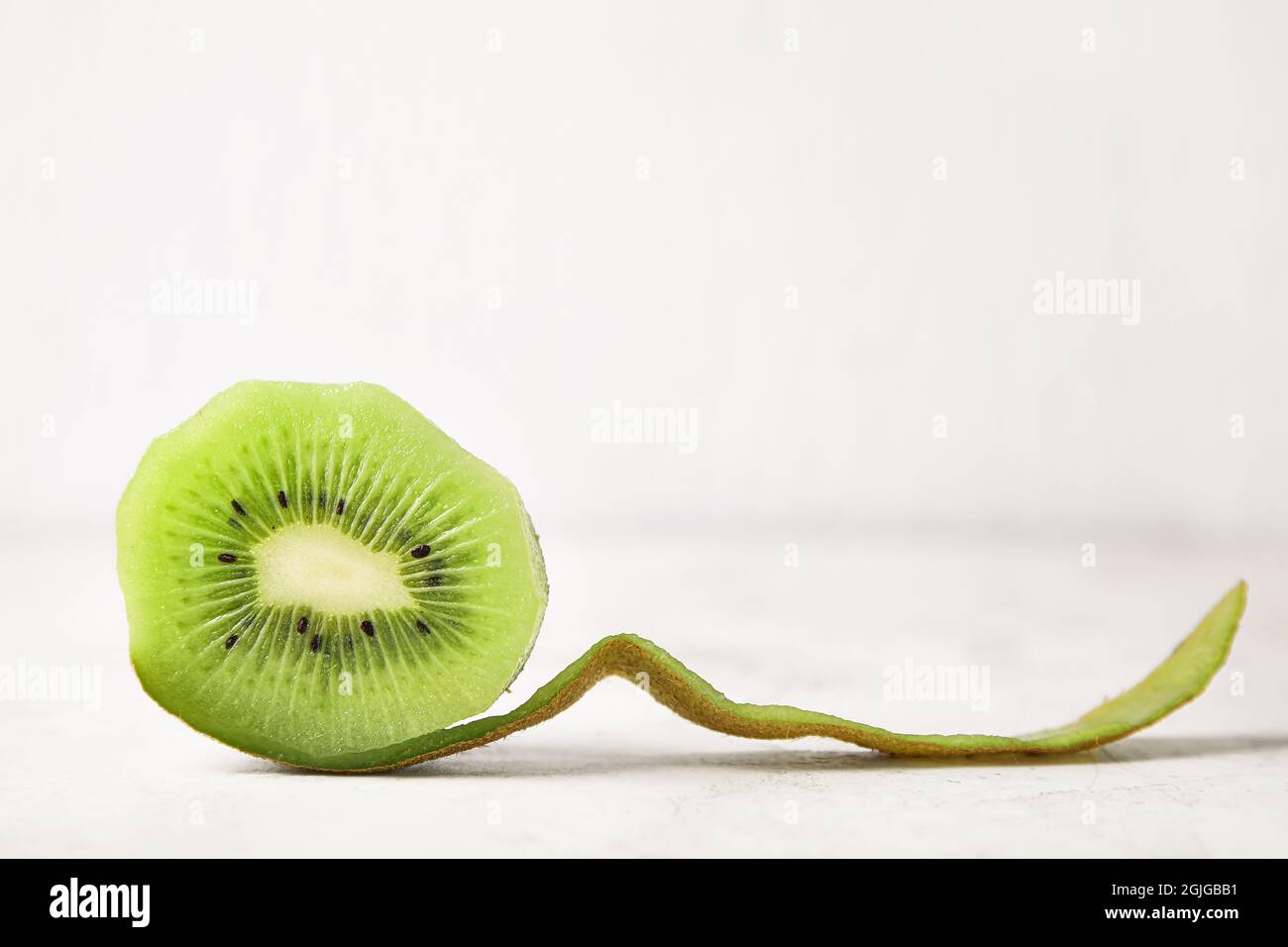 Slice of fresh kiwi fruit with peel on light background Stock Photo - Alamy
