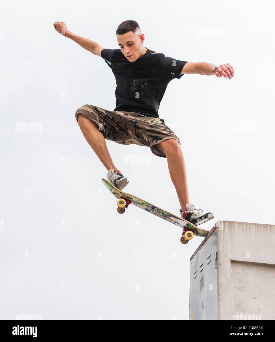 Vertical shot of a skateboarder in shorts jumping a wall in an urban ...