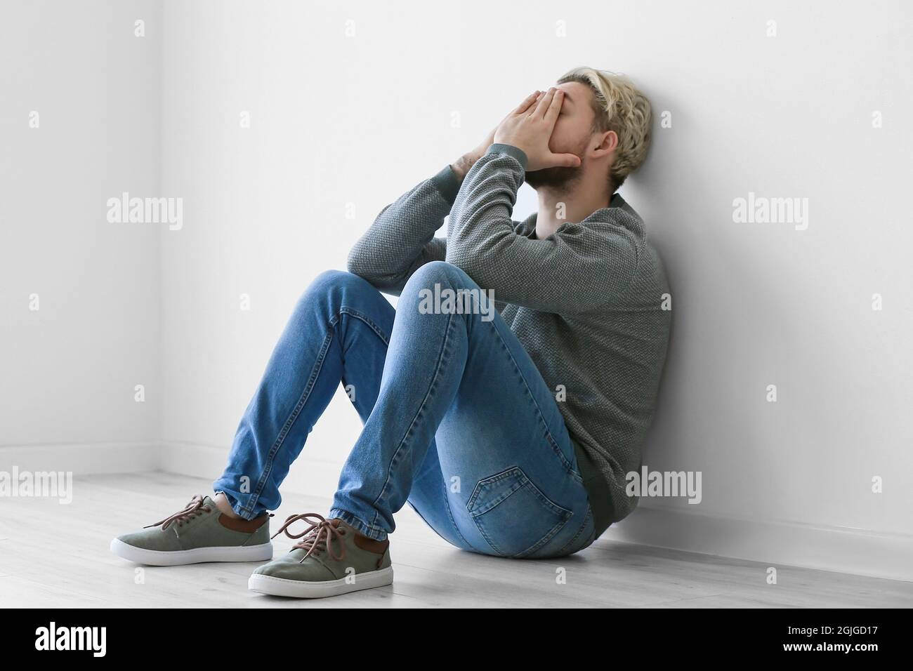 Depressed young man sitting near light wall Stock Photo - Alamy