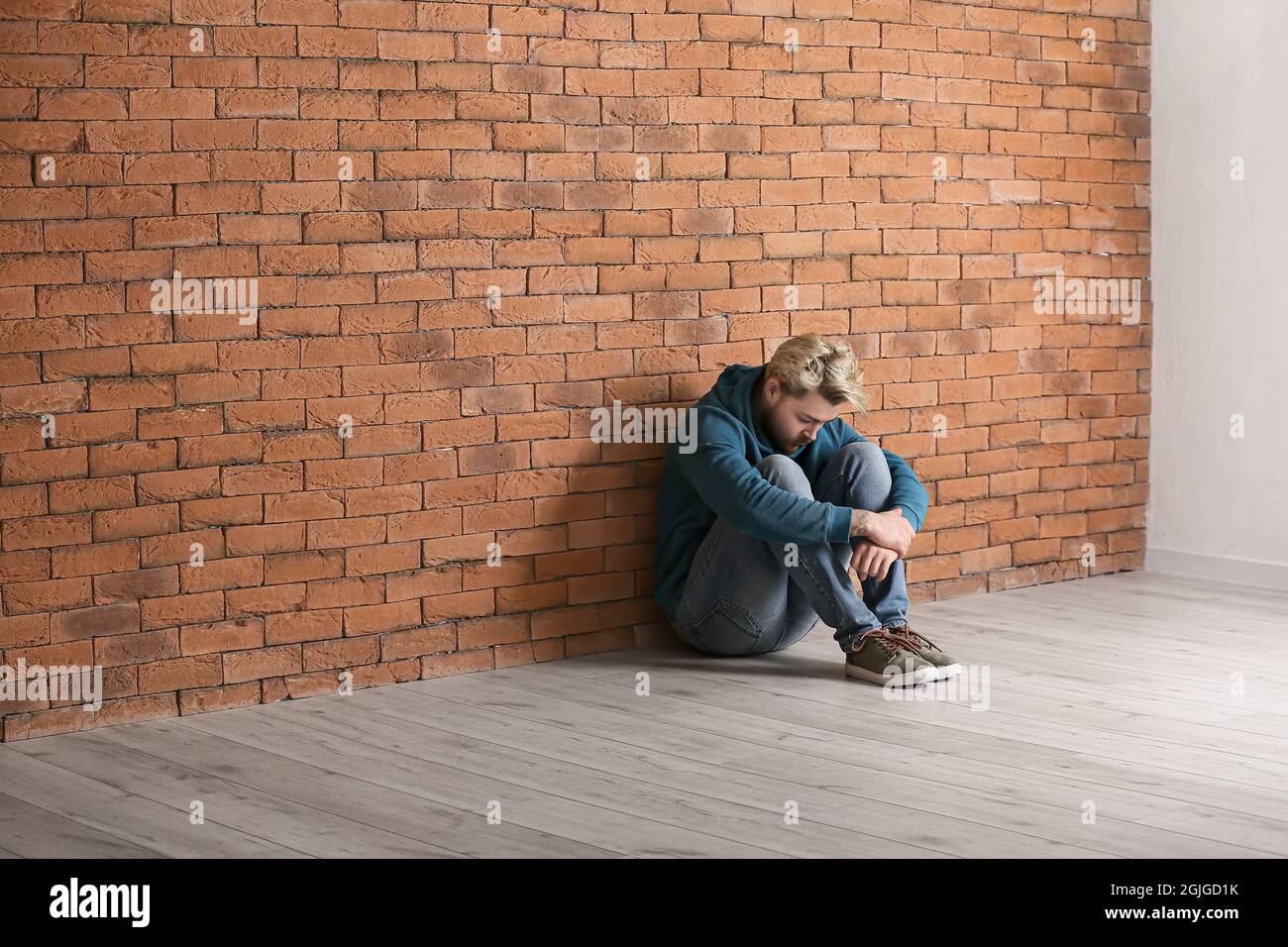 Depressed young man sitting near brick wall Stock Photo - Alamy
