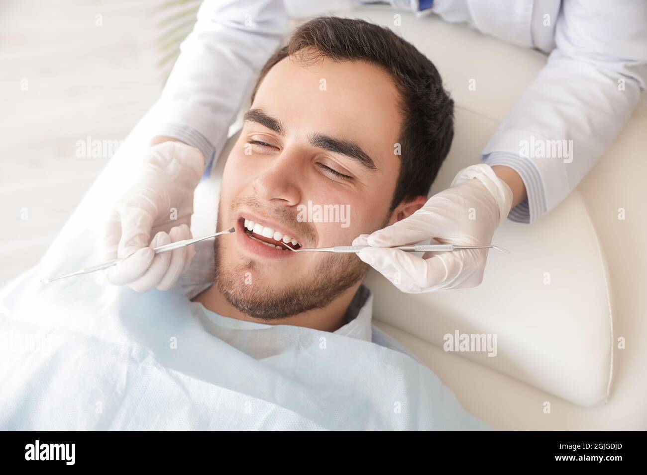 Dentist examining teeth of young man in clinic Stock Photo - Alamy