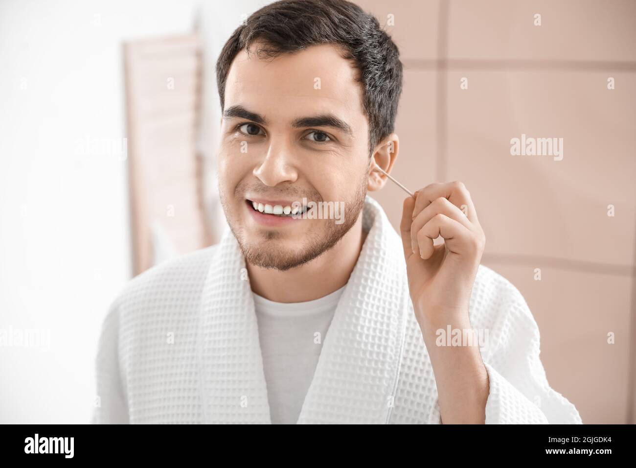 Young man cleaning ears with cotton bud in bathroom Stock Photo - Alamy