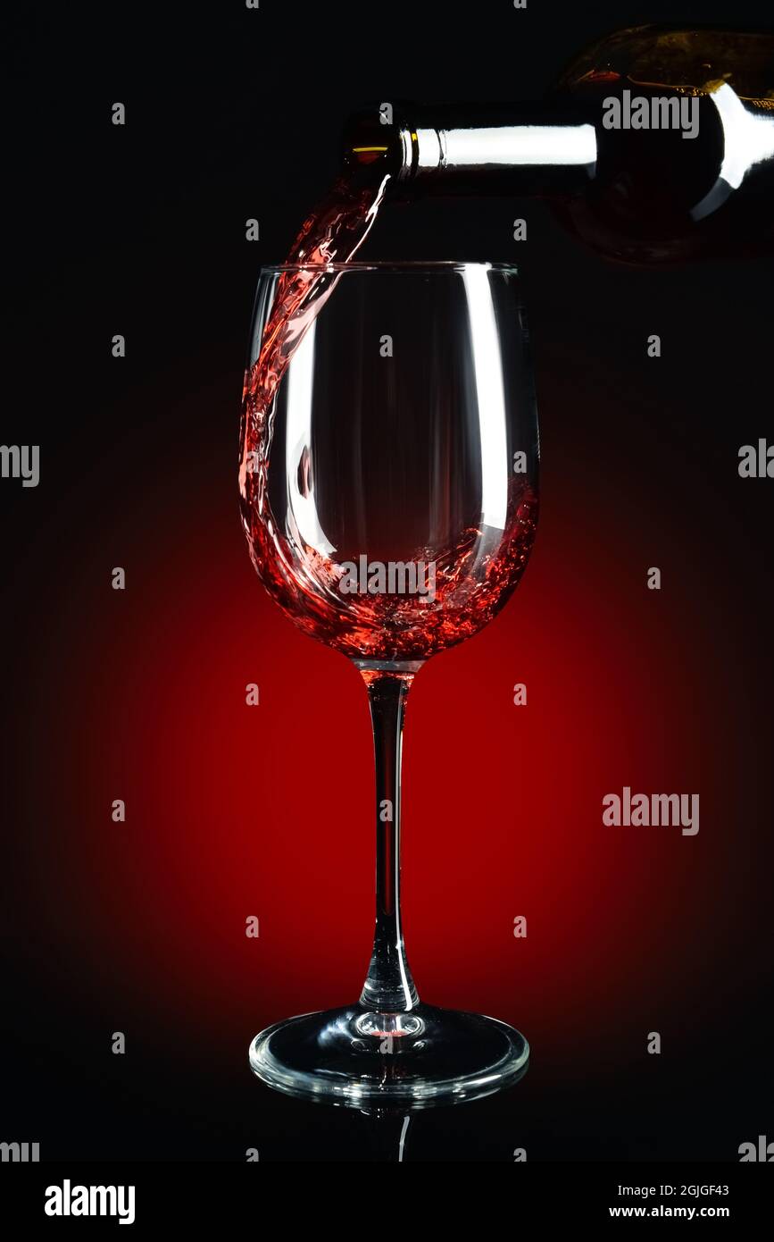 Pouring of red wine into glass on dark background Stock Photo - Alamy