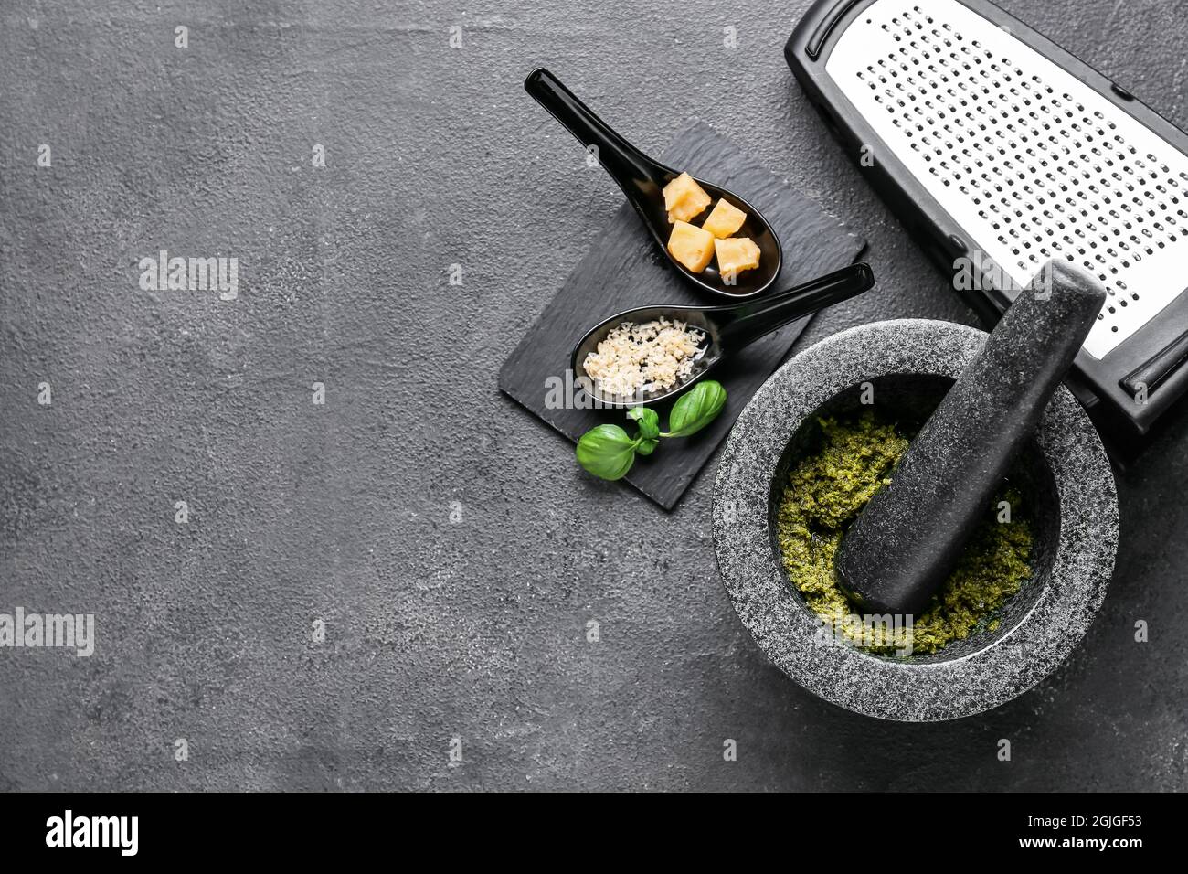 Mortar with tasty pesto sauce, cheese and grater on dark background ...