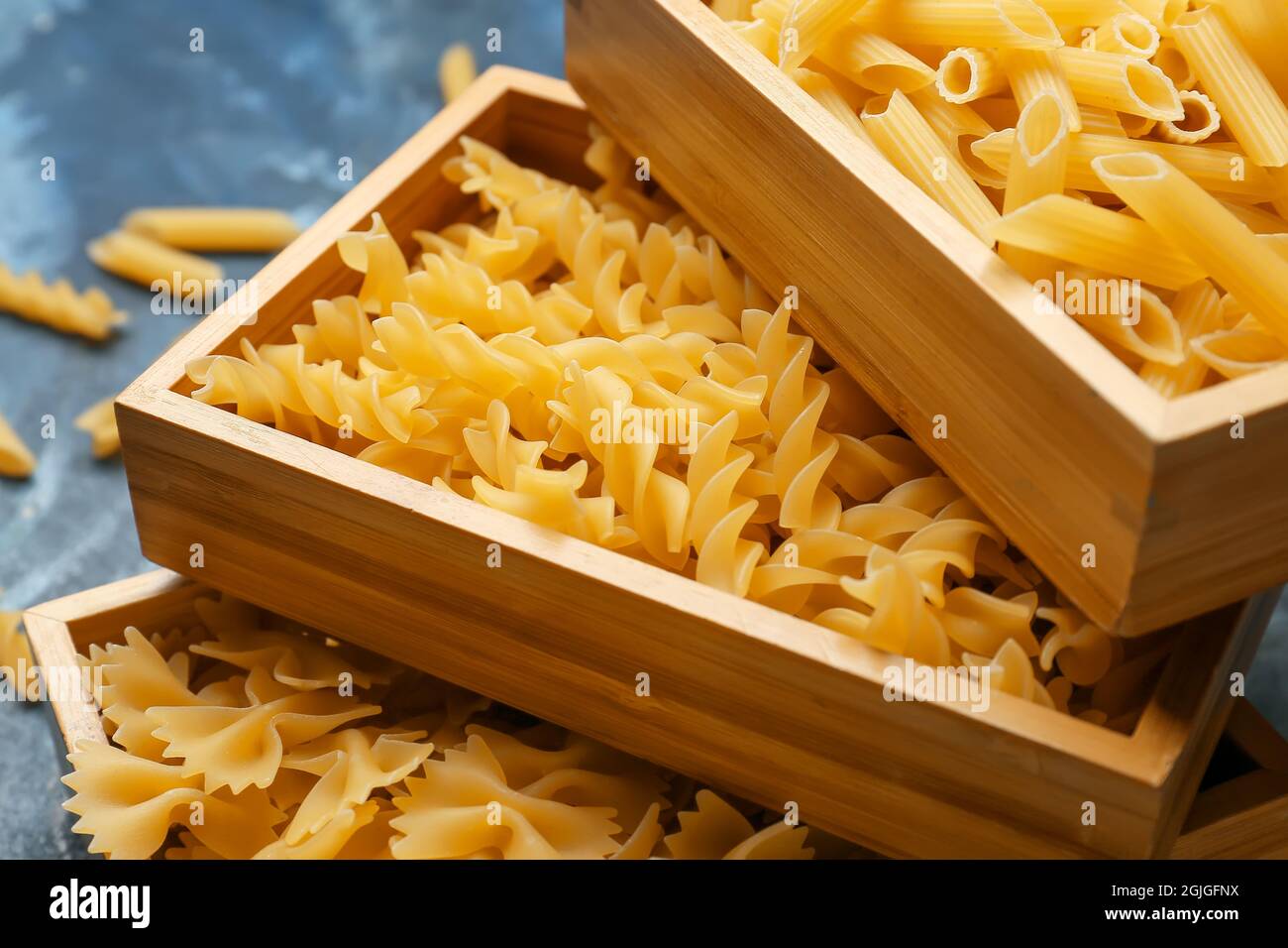 Wooden boxes with different types of uncooked pasta on color background ...