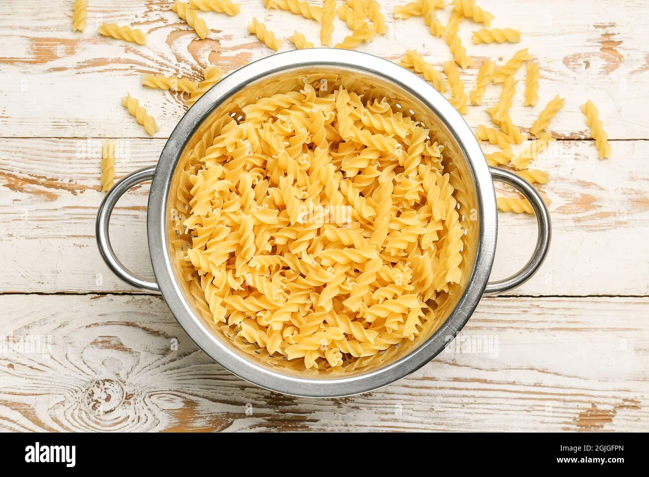Colander with uncooked fusilli pasta on wooden background Stock Photo ...
