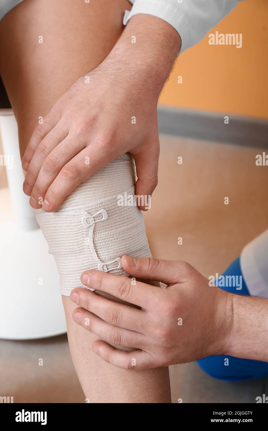 Doctor applying bandage onto knee of young woman near color wall Stock ...