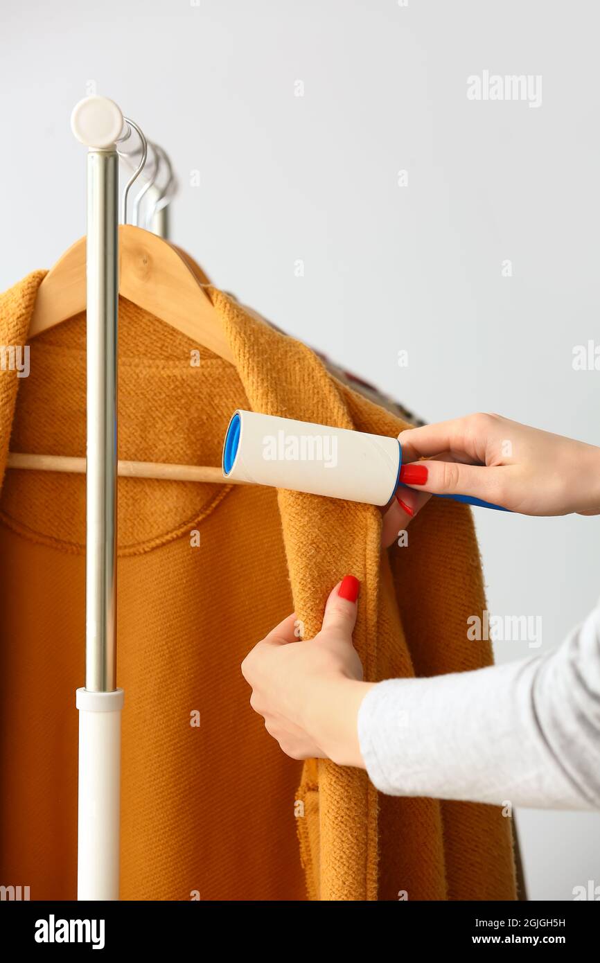 Woman cleaning coat with lint roller on light background Stock Photo ...