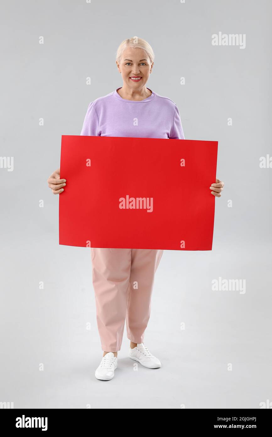 Mature woman with blank poster on light background Stock Photo - Alamy