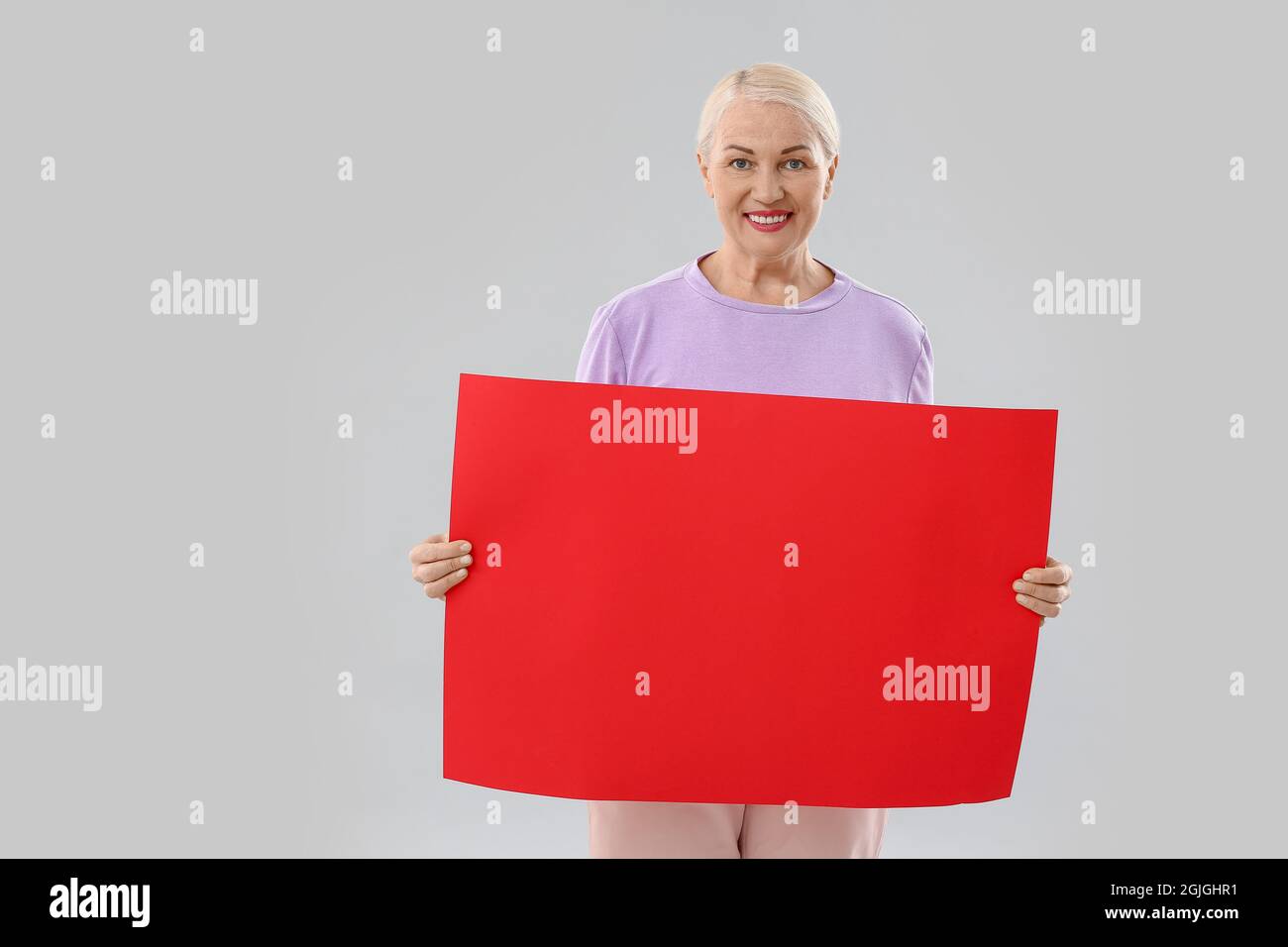 Mature woman with blank poster on light background Stock Photo - Alamy