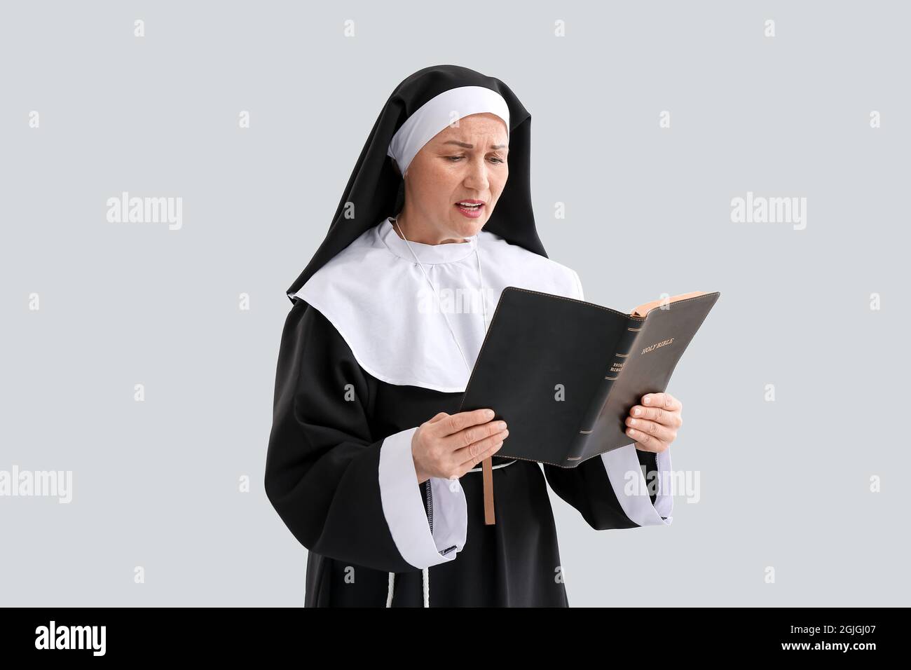 Mature nun reading Holy Bible on light background Stock Photo - Alamy