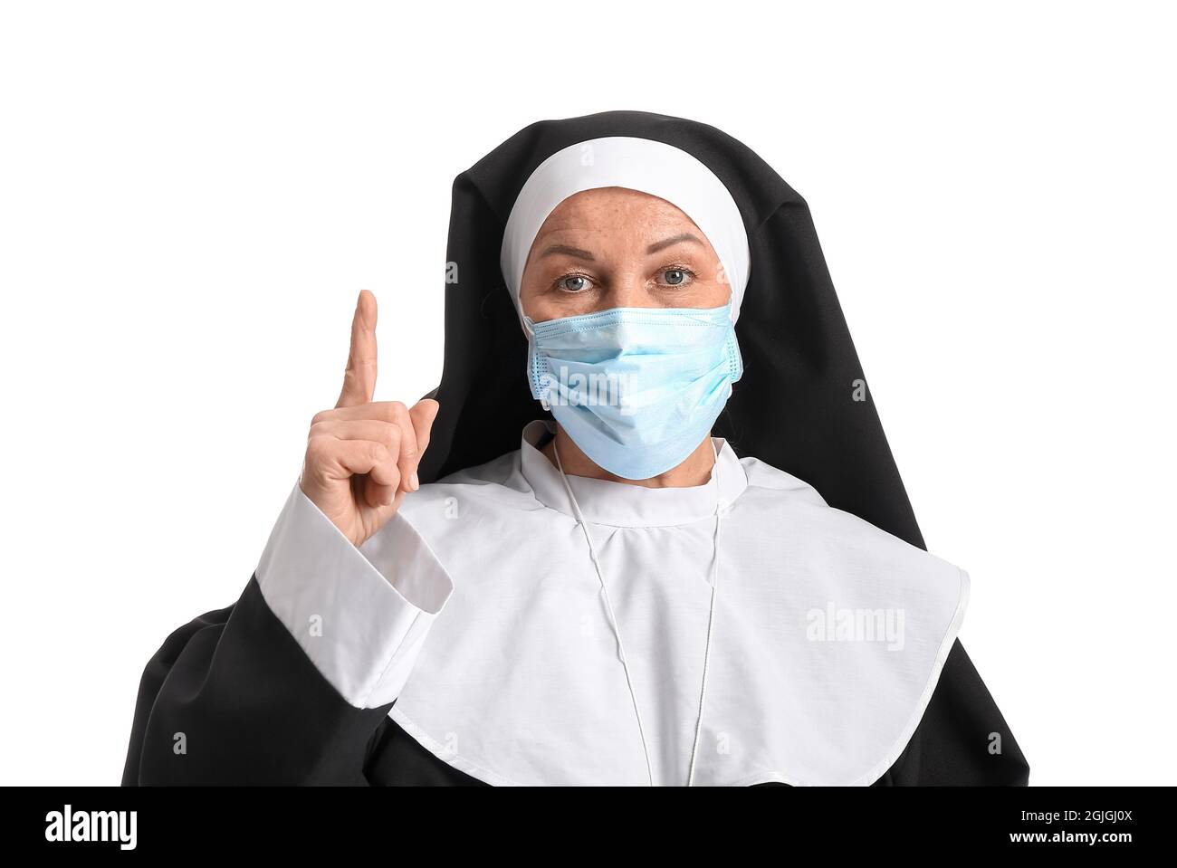Mature nun in medical mask with raised index finger on white background ...