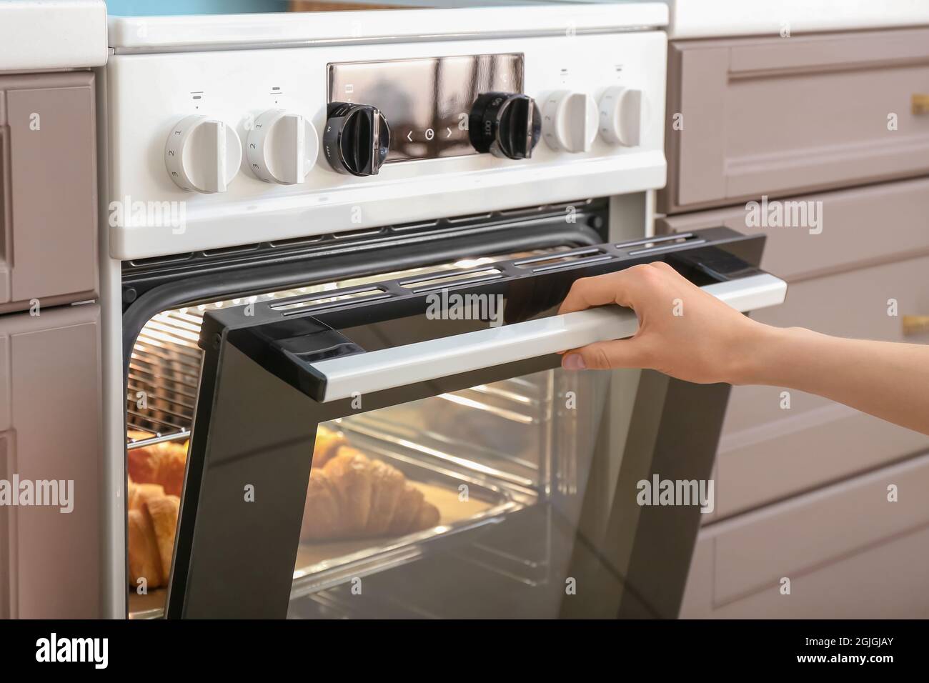 Woman opening oven with croissants in kitchen Stock Photo - Alamy