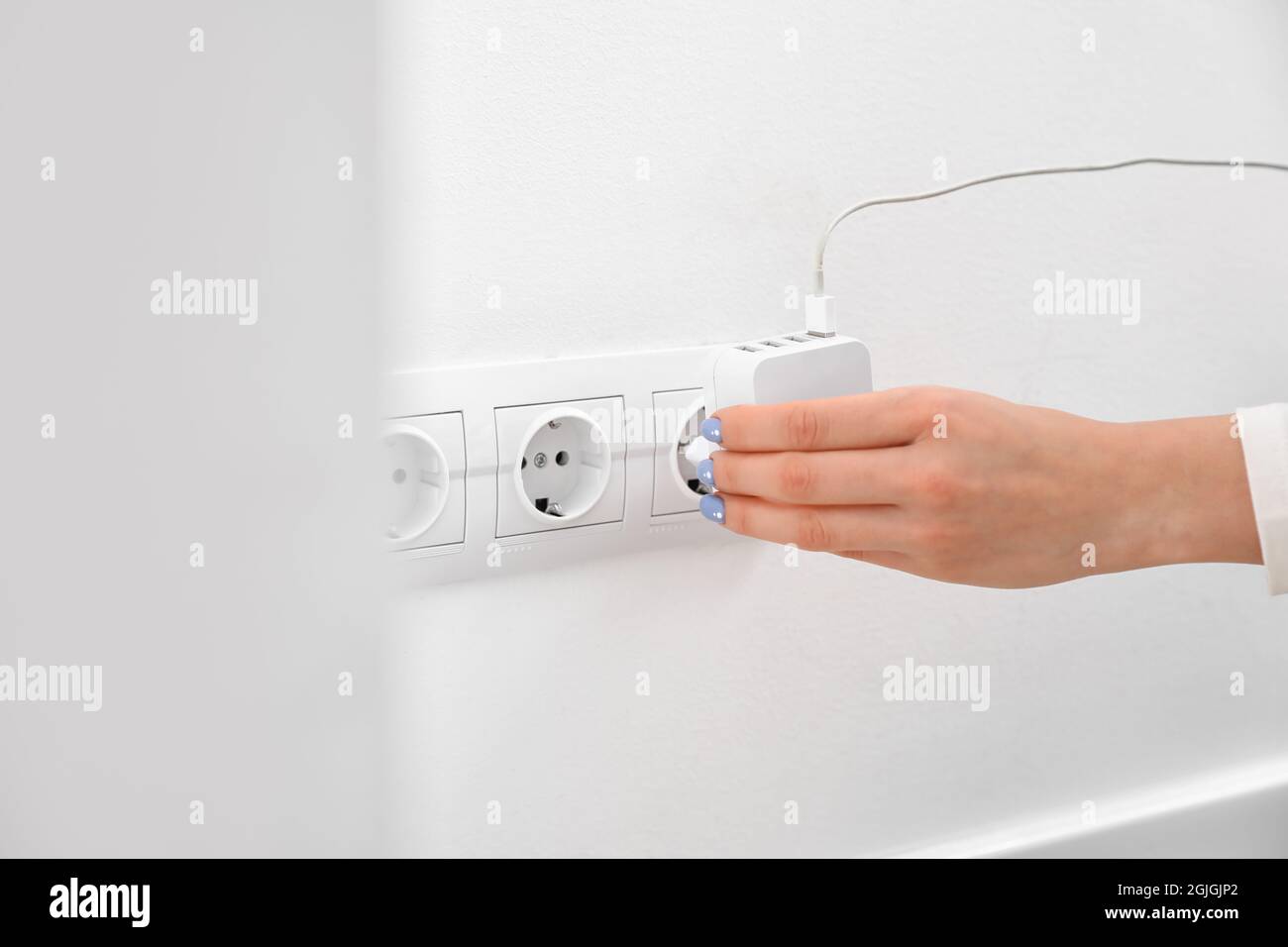 Woman putting plug into socket in room Stock Photo - Alamy