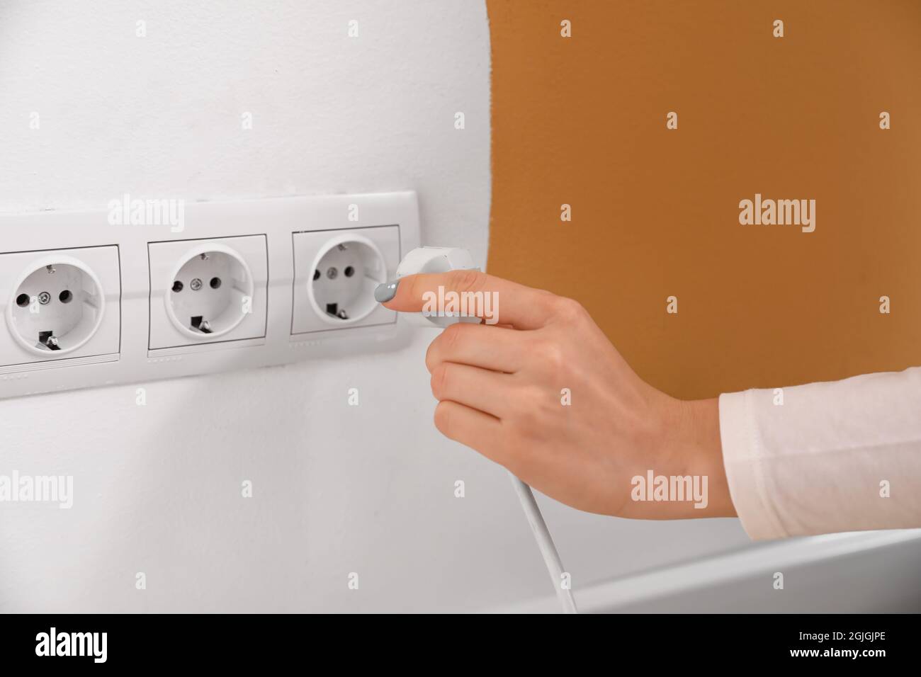 Woman putting plug into socket in room Stock Photo - Alamy
