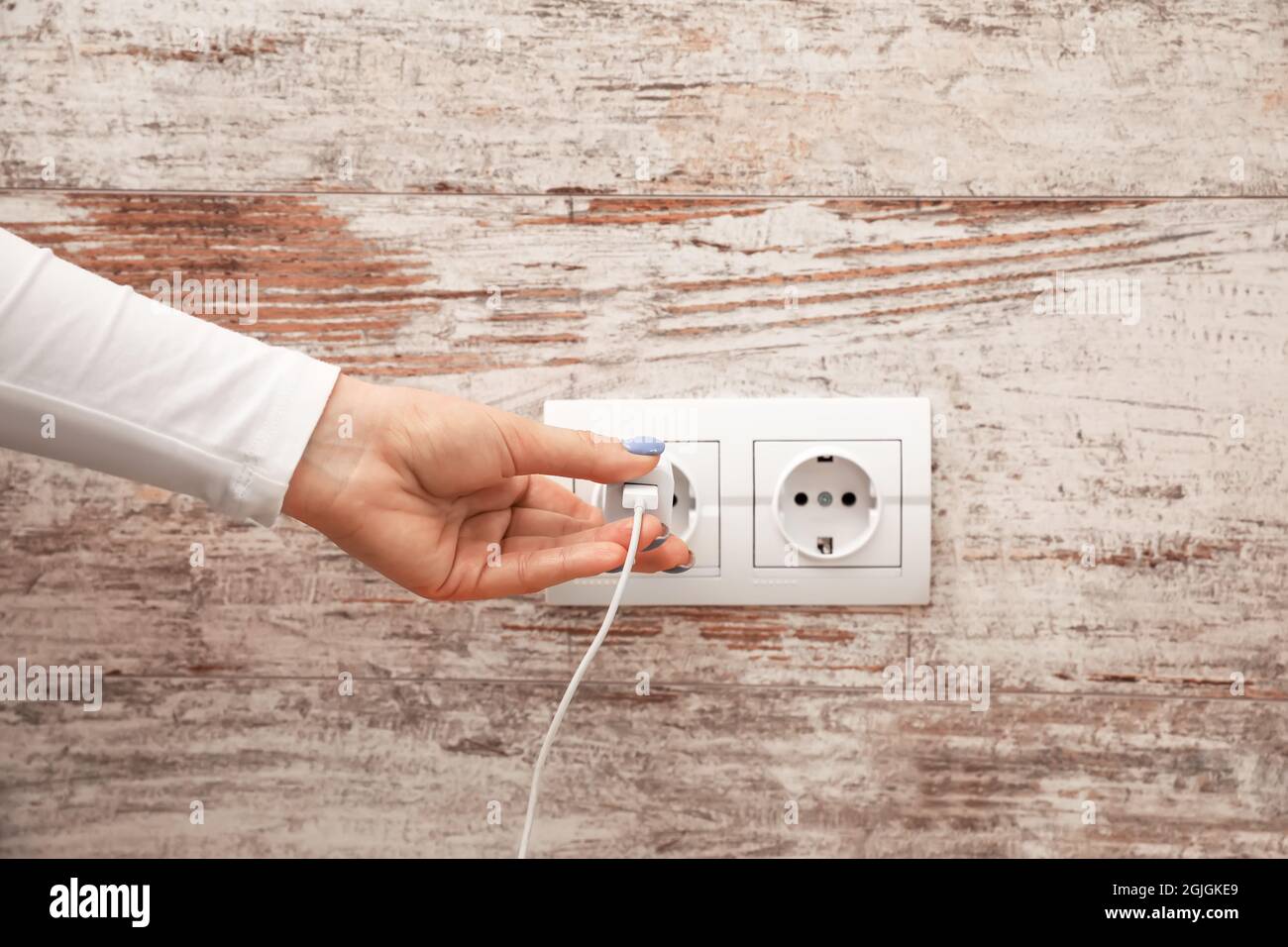 Woman inserting plug into socket on wooden wall Stock Photo - Alamy
