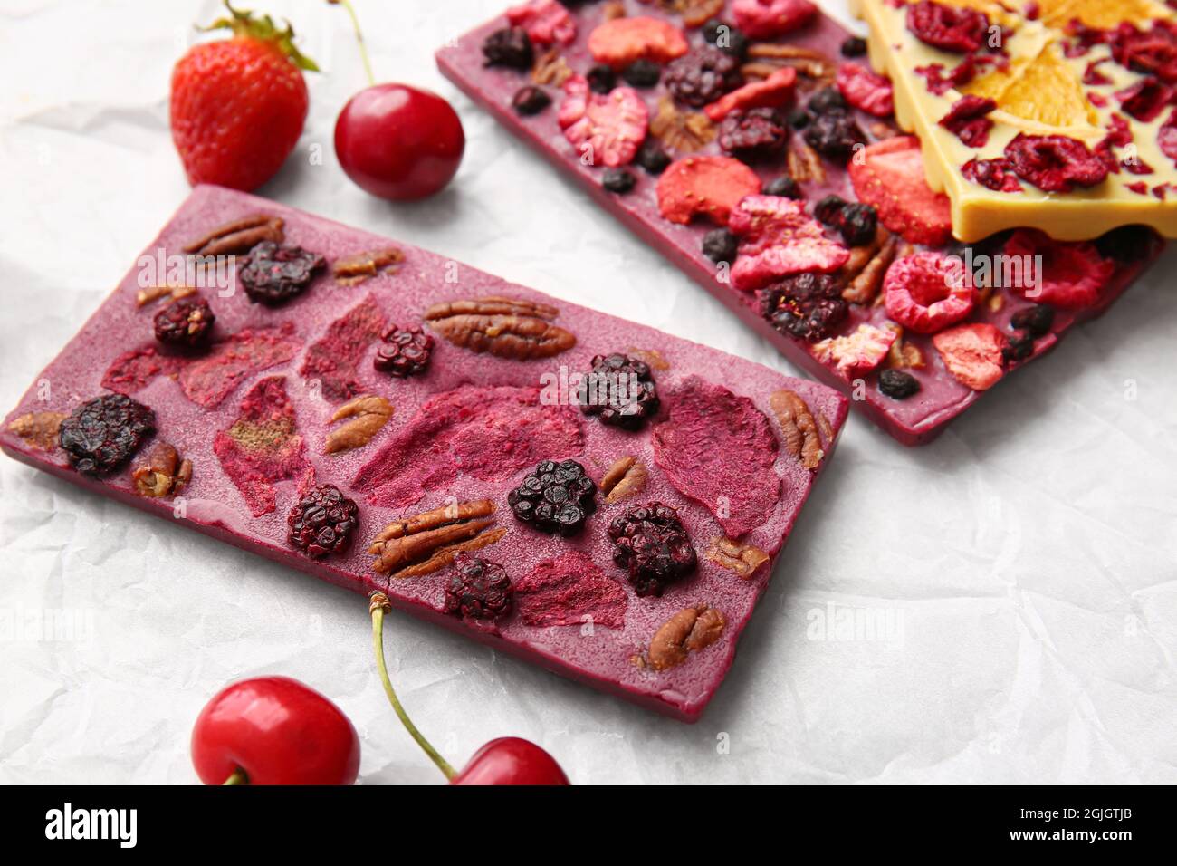 Handmade chocolate bars with fruits, berries and nuts on parchment ...