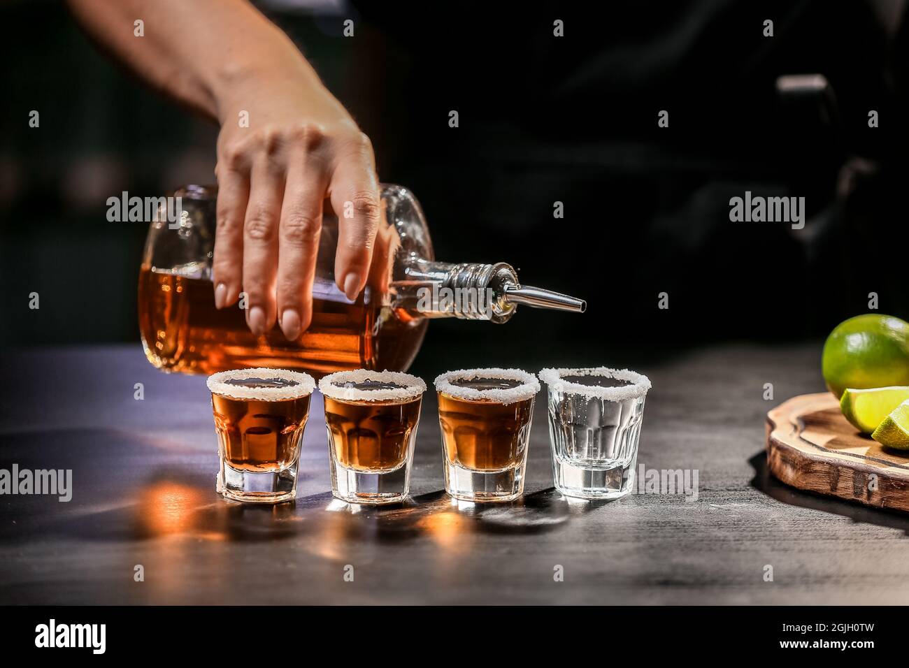 Bartender pouring tasty tequila into glasses on dark background Stock ...