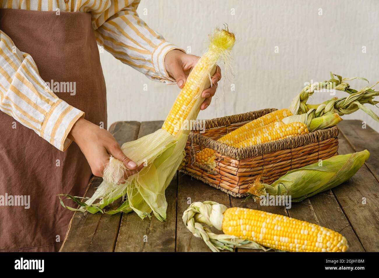 Woman peeling corn cob on wooden table Stock Photo - Alamy