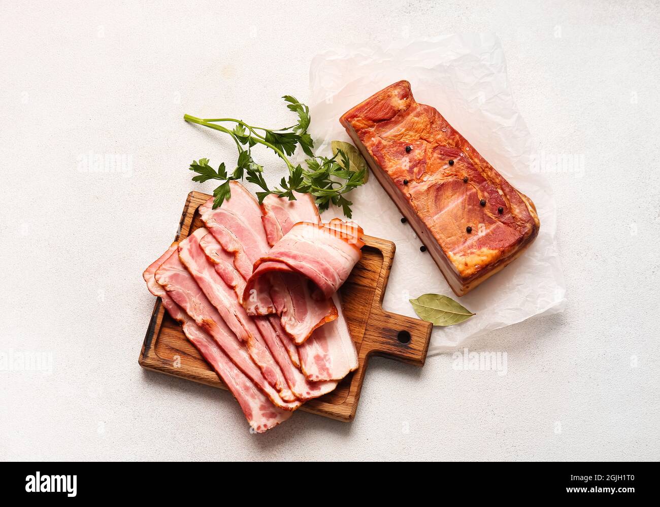 Wooden board with slices of tasty smoked bacon on light background ...