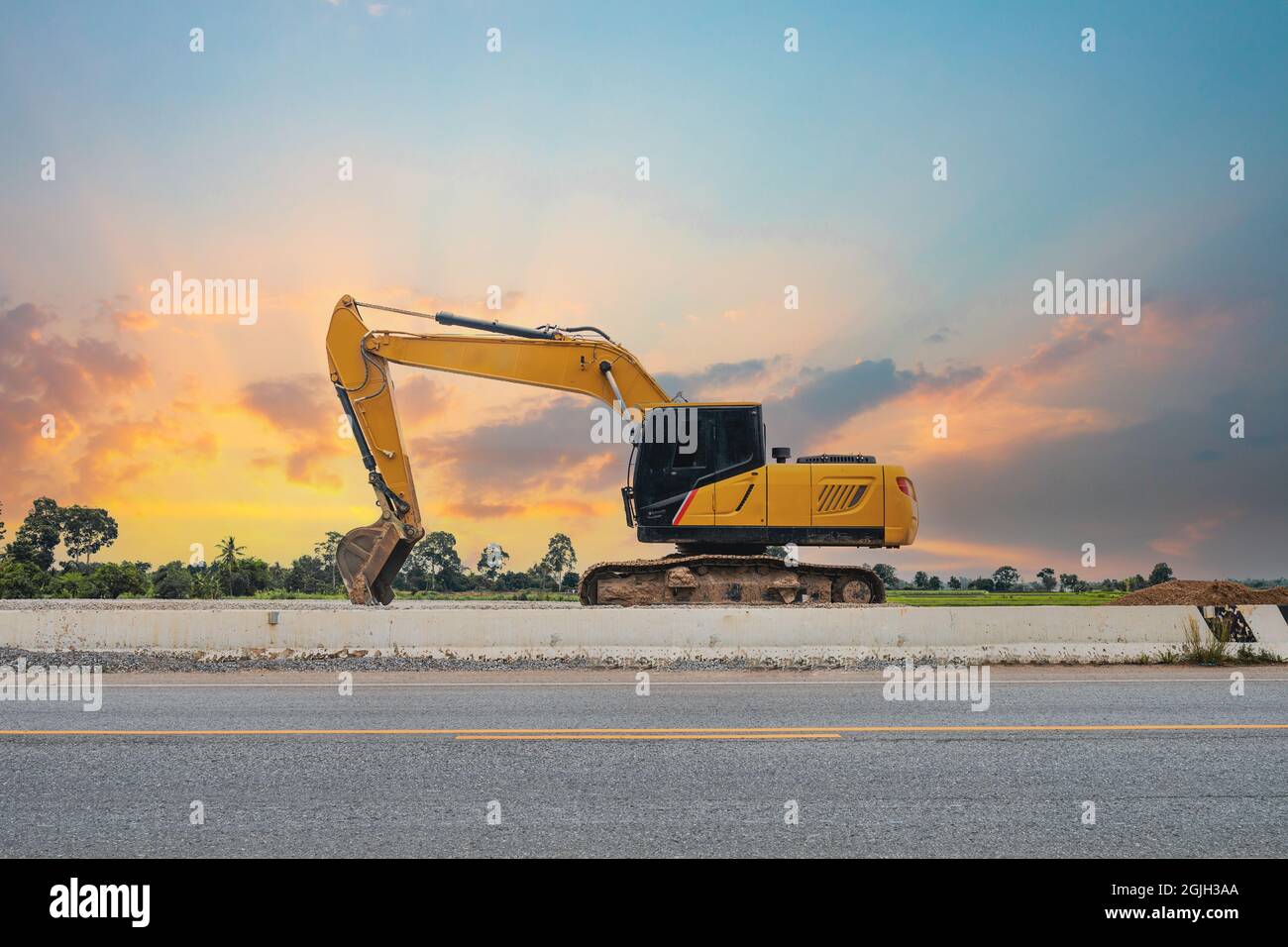 A yellow backhoe parked on the roadside in the sky at sunset Stock ...