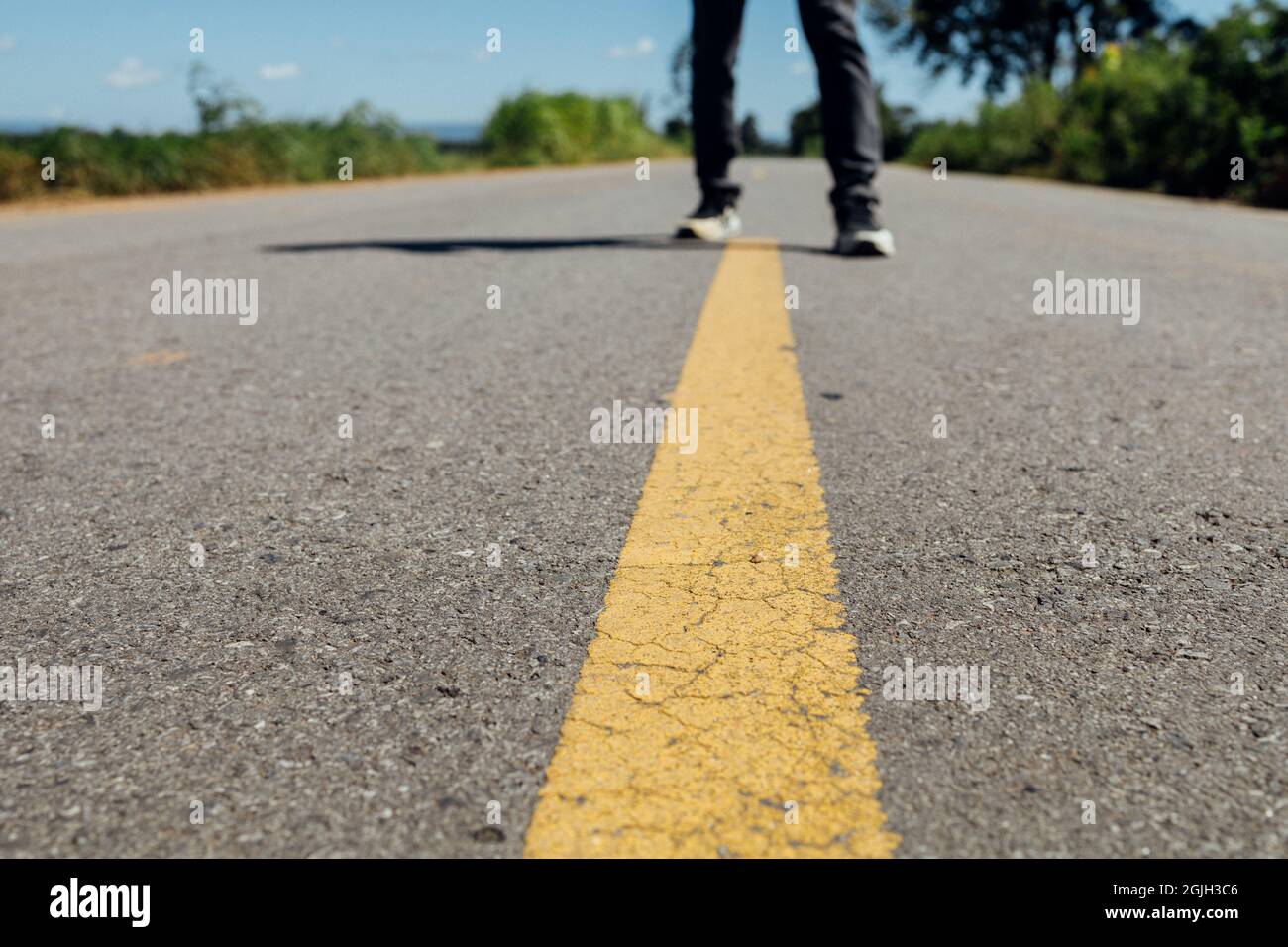 Men`s feet standing on asphalt road with yellow marking lines. Man ...