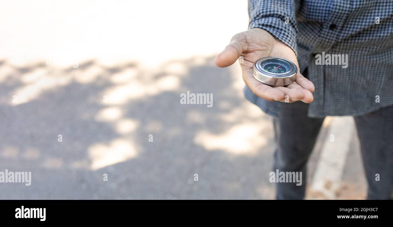 Male traveler holding a magnetic compass on asphalt road, orientation ...
