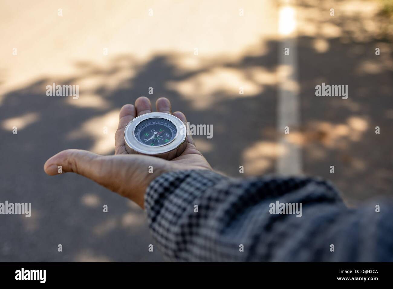 Male traveler holding a magnetic compass on asphalt road, orientation ...