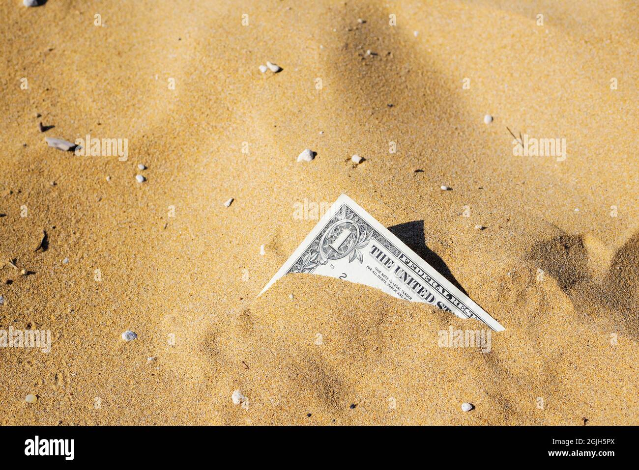 Top view of one dollar banknote corner buried in the sand. Copy space ...