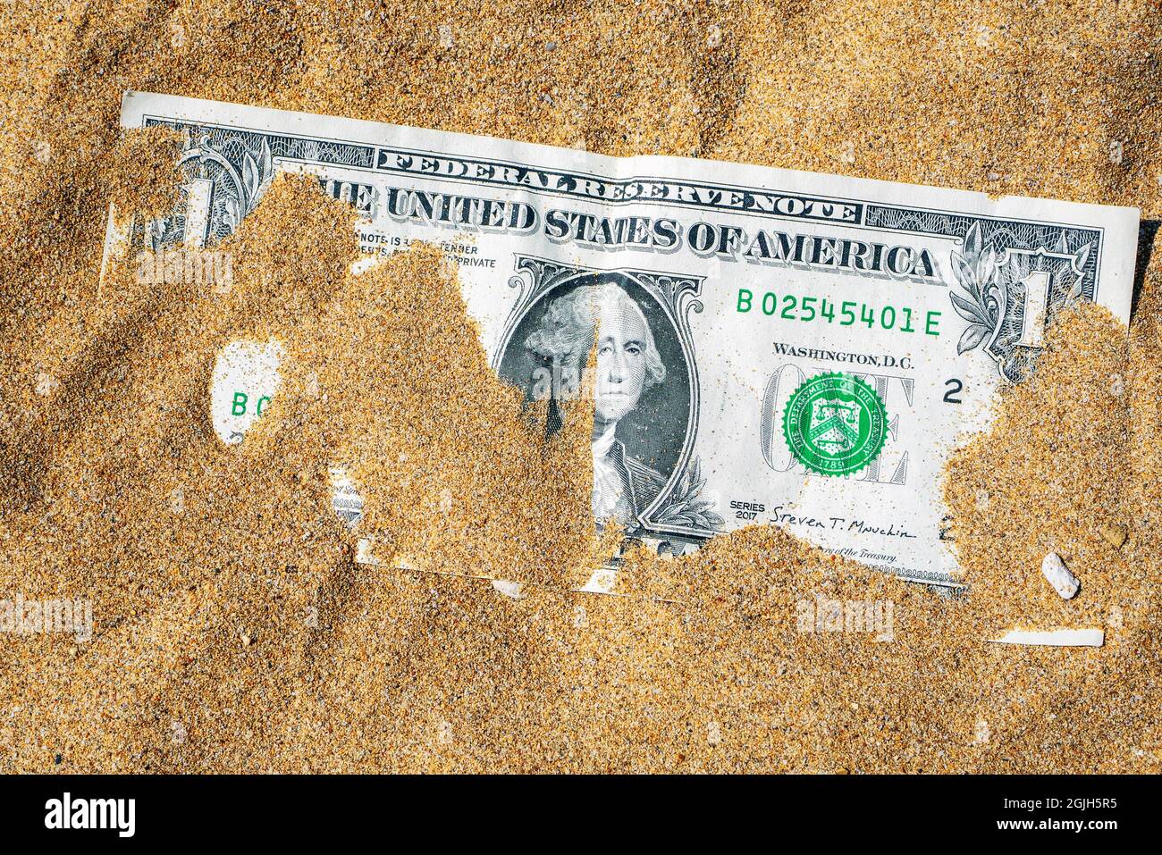 Top view of one dollar banknote buried in the sand. Closeup of dollar ...